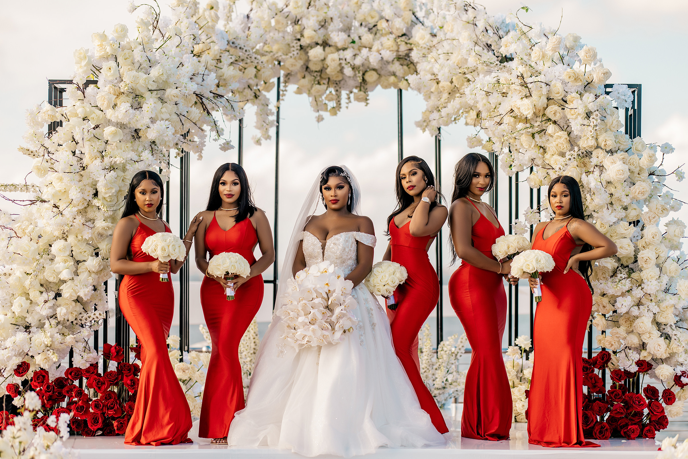 Group shot of bridesmaids in red with bride under giant floral arbor ...