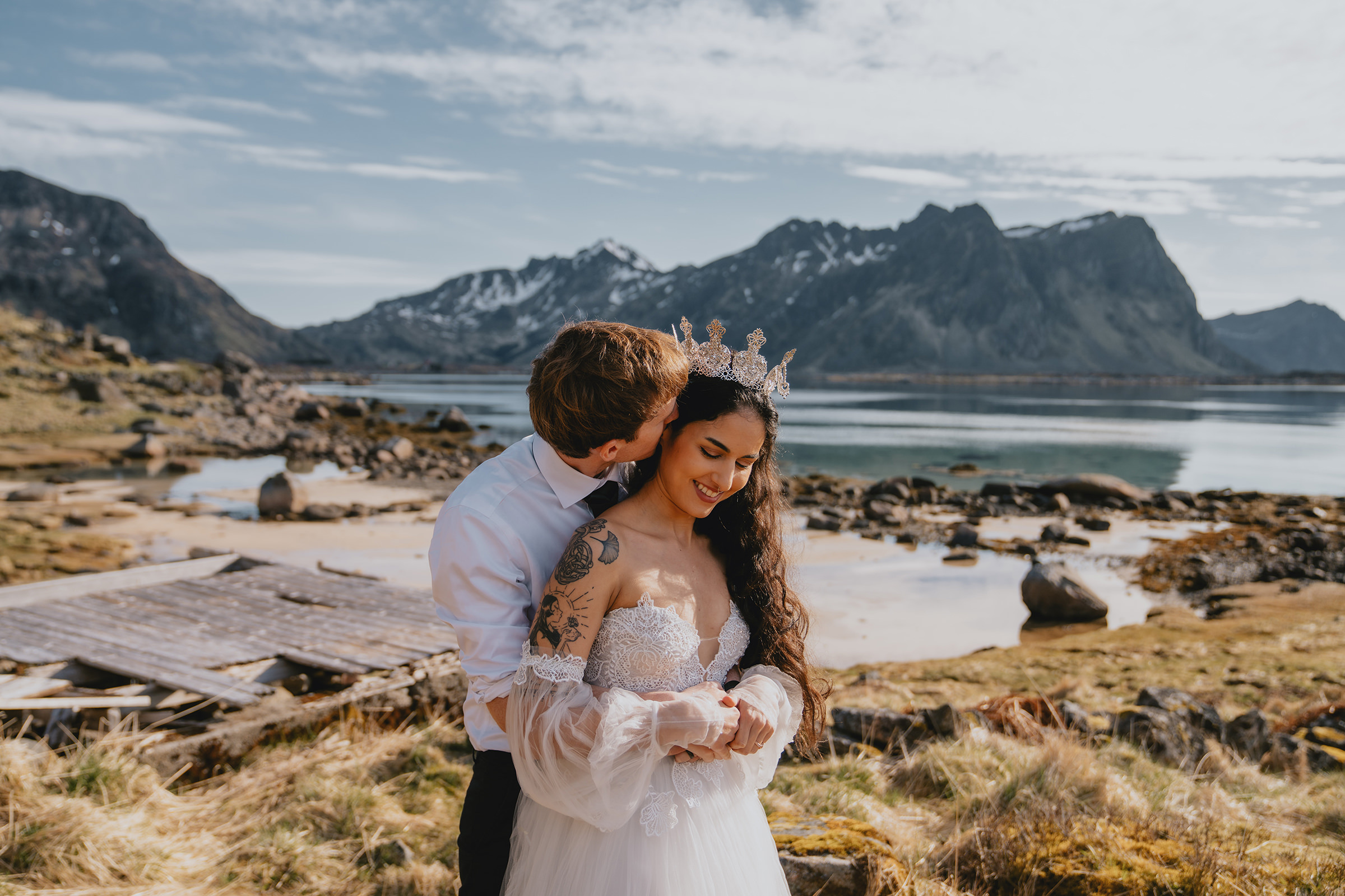 Groom kisses tattooed bride wearing crown against epic scenery Lofoten ...