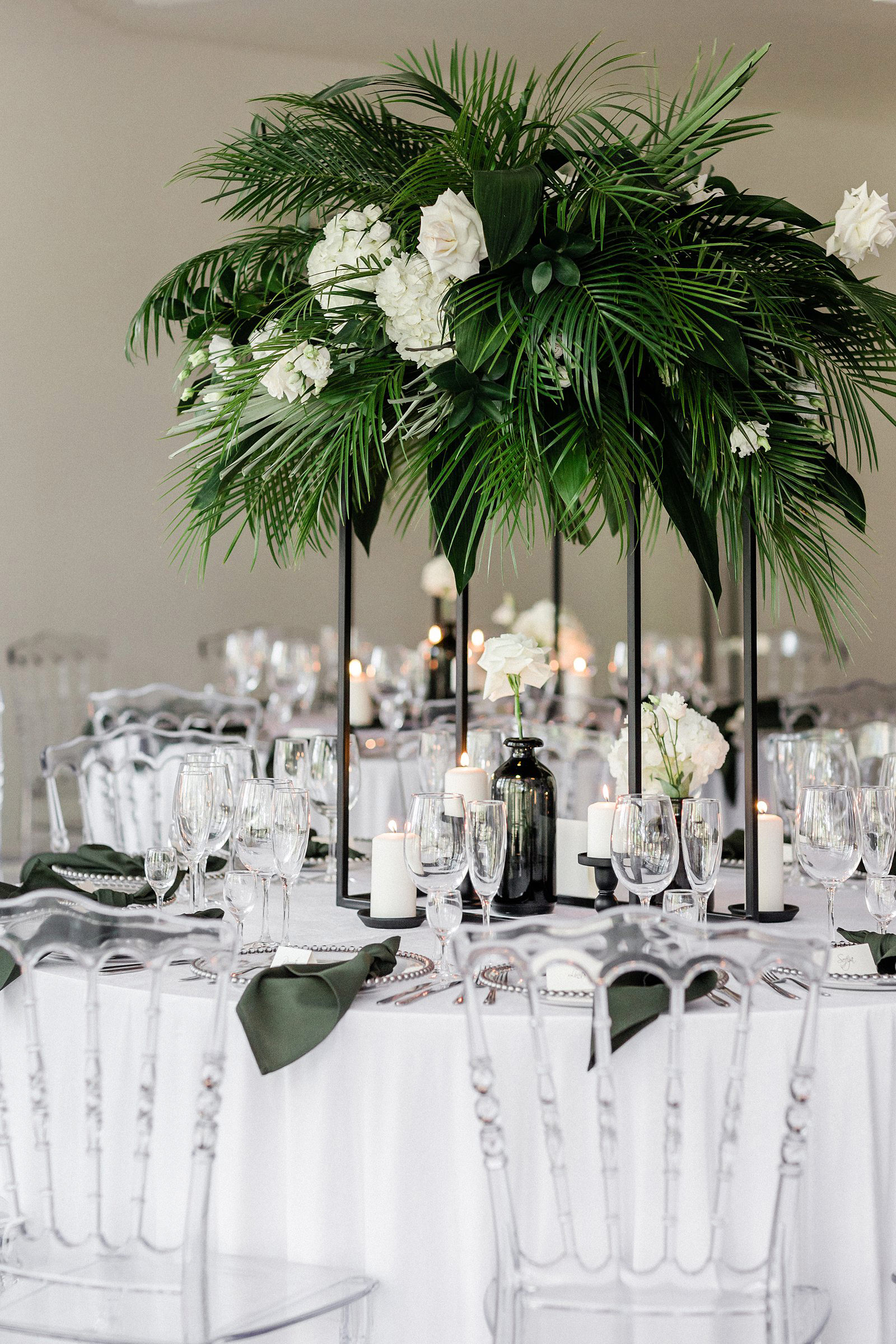tall table centerpiece of tropical green leaves and white roses with ...